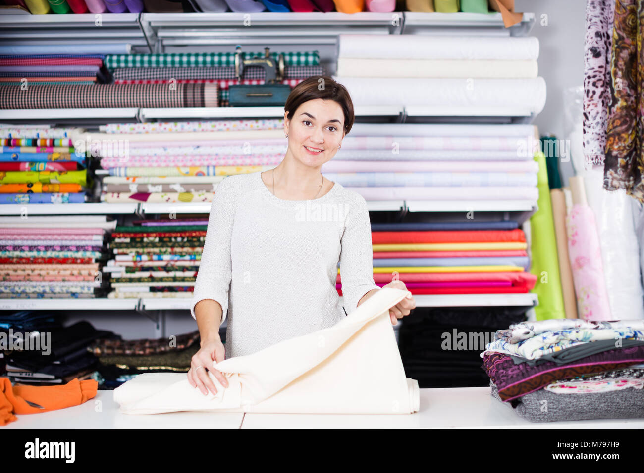 Female shop assistant demonstrating white fabric at drapery shop Stock ...