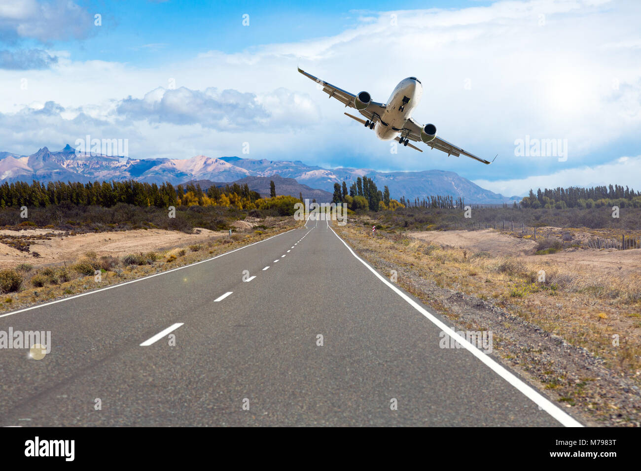 Airplane flying over roadway on background mountains and cloudscape ...