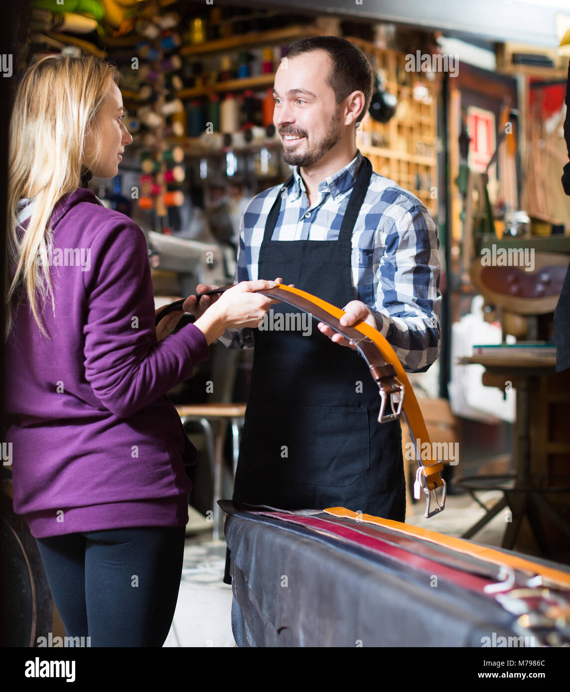 Young man worker assisting female customer in choosing belt in leather ...