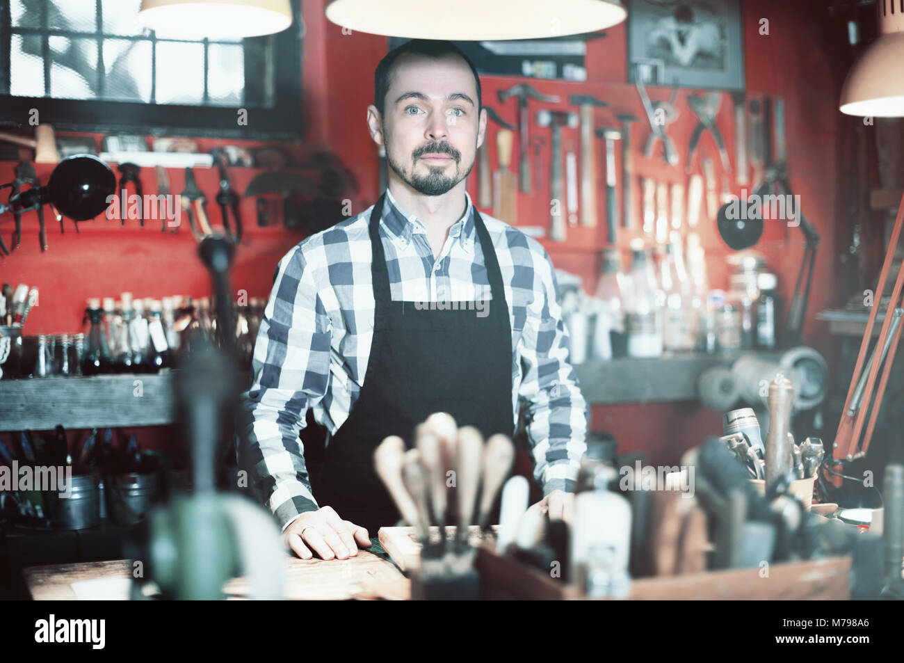 Positive male worker showing his workplace and tools in leather ...