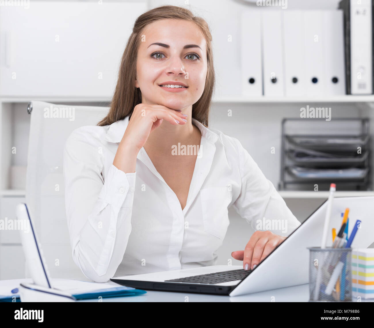 Office female worker is posing while working behind laptop in the ...
