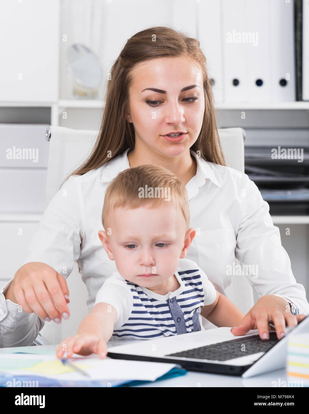 Girl with kid is working behind laptop in office Stock Photo - Alamy