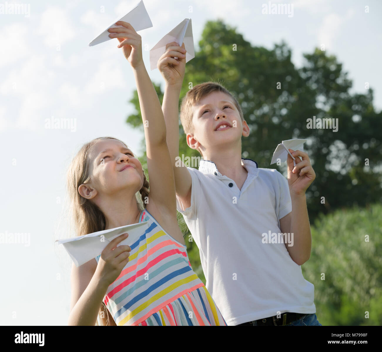 Two joyful smiling children playing with flying paper planes outdoors ...