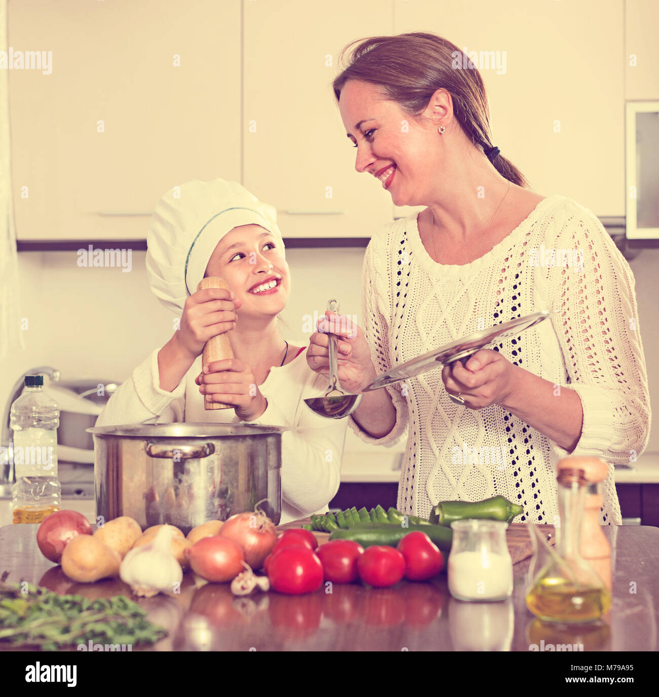 Happy smiling mother and her cheerful daughter preparing soup together ...