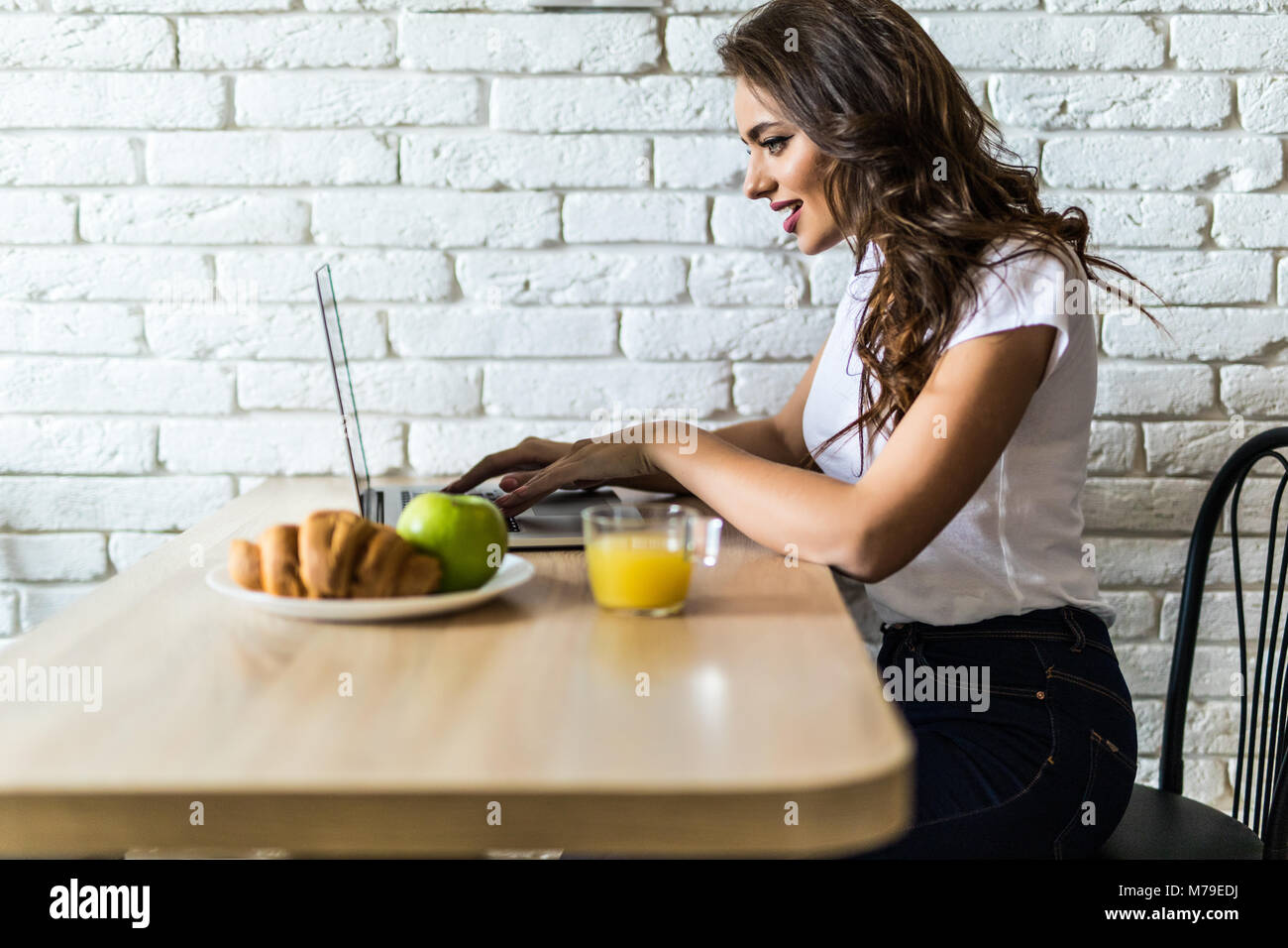 Young cheerful woman using on laptop computer and eating fruits in the ...