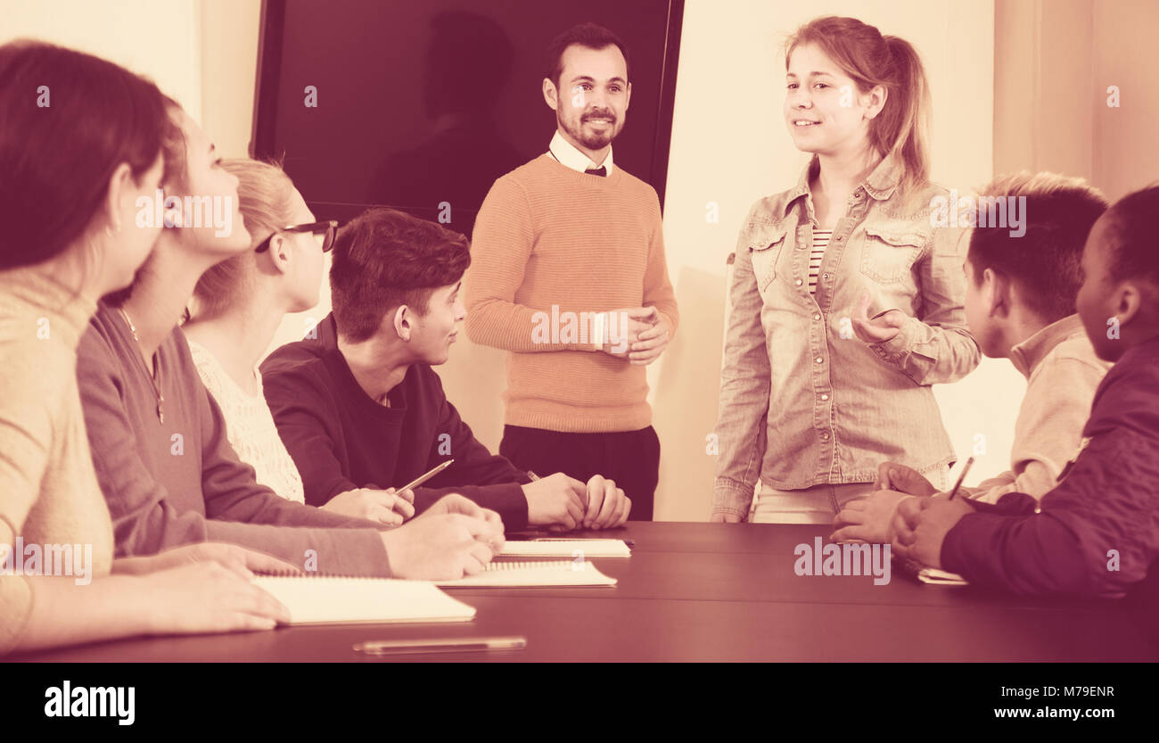 Young teenager girl is giving answer to teacher’s question at writing ...