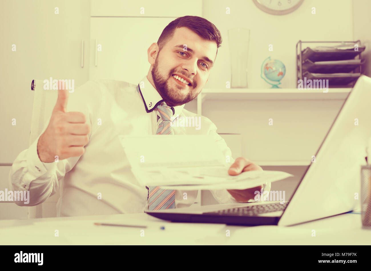 Young cheerful positive male worker working productively on project in ...
