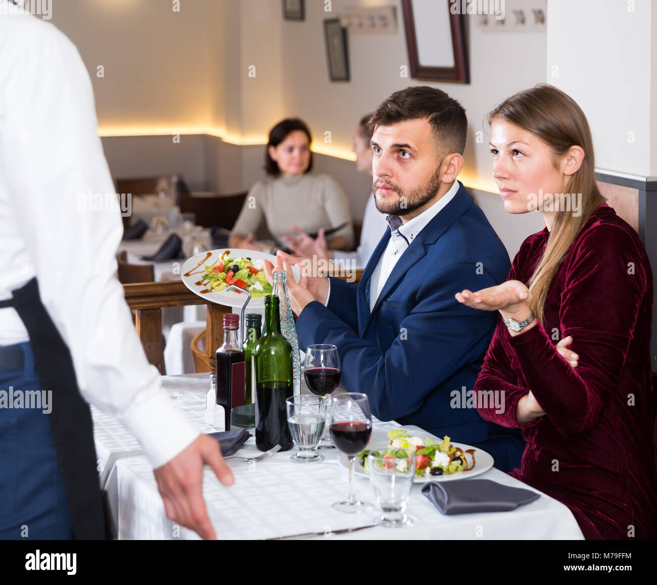 scowling guests conflicting with waiter because of poor quality of dish ...