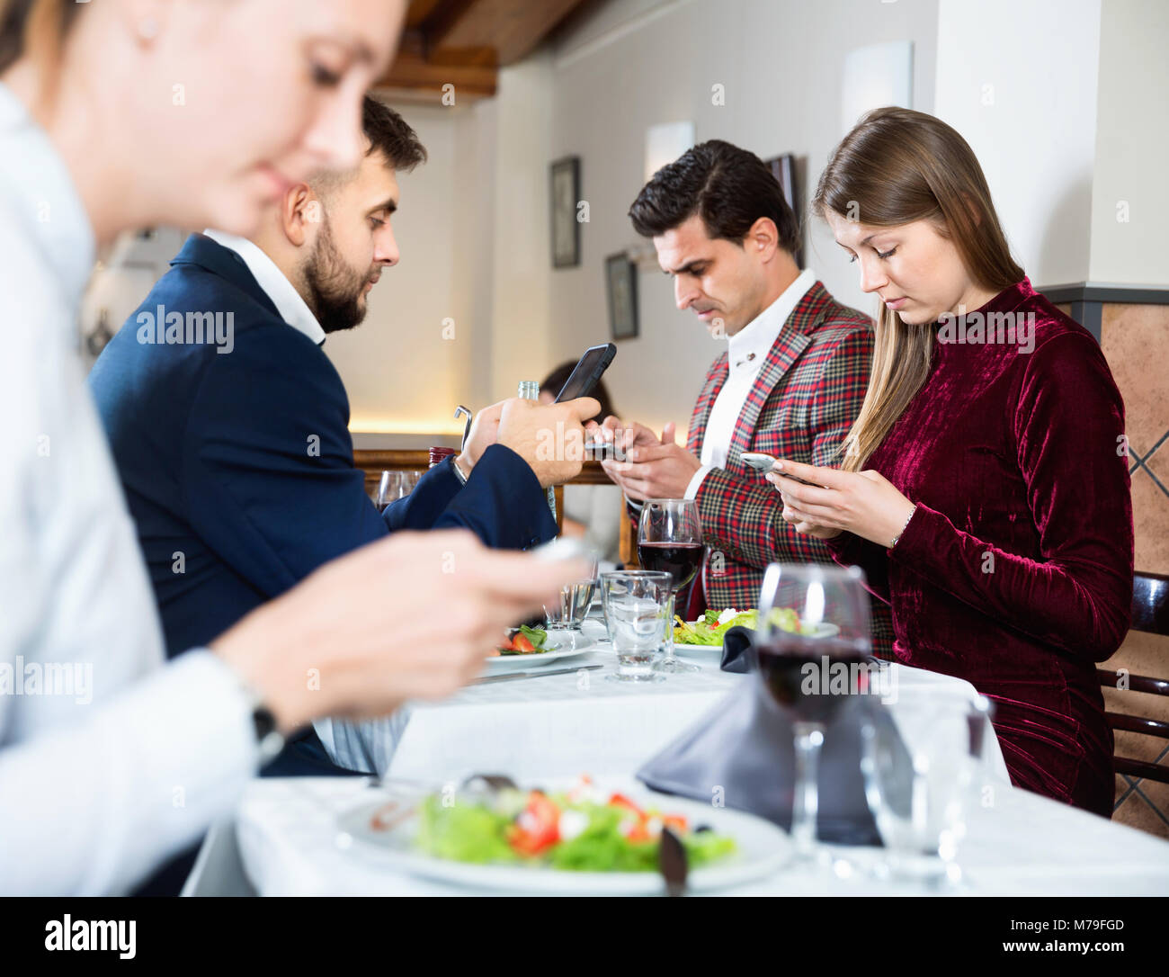 Modern cheerful positive people busying with phone during evening meal ...