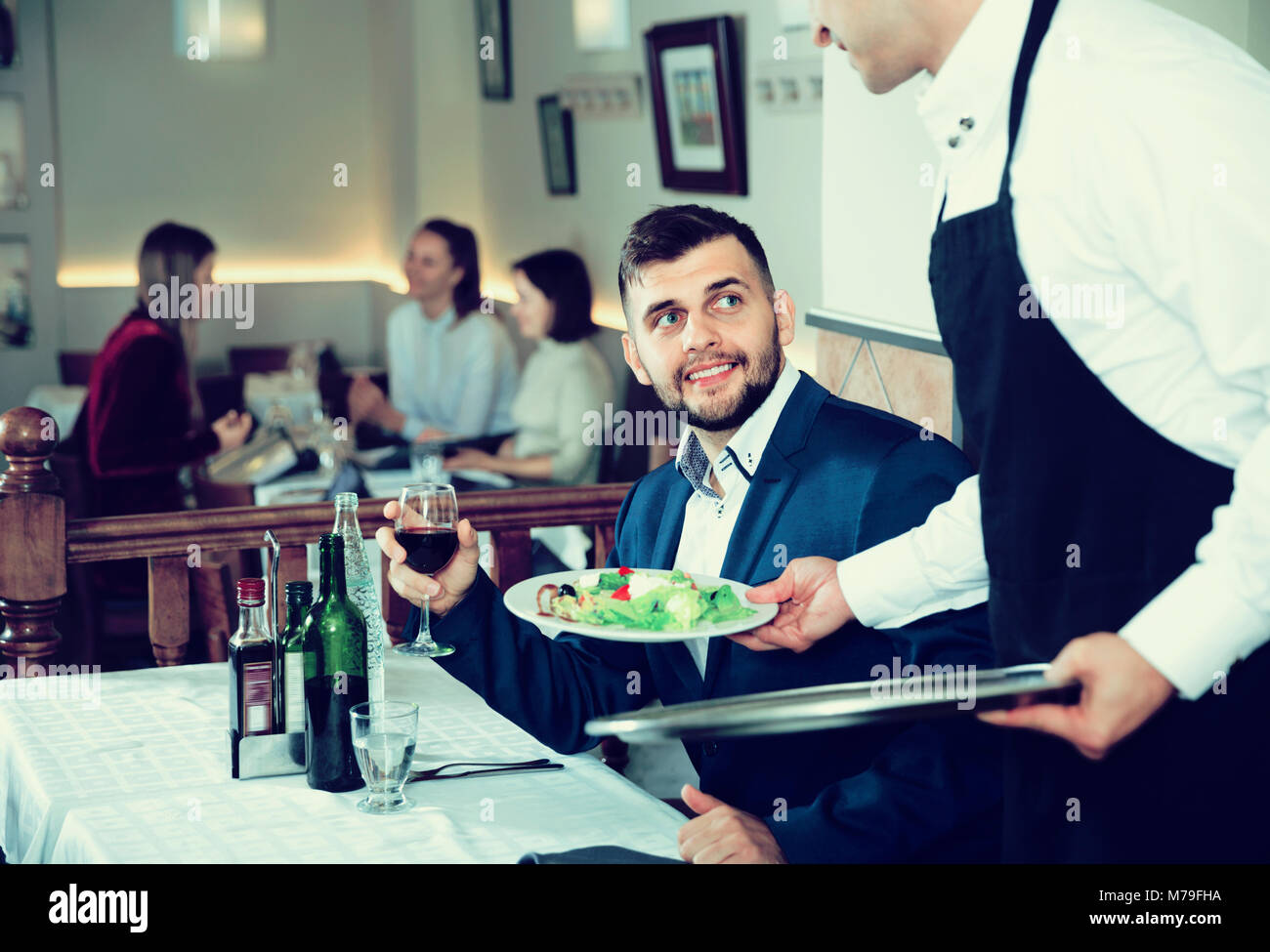 Glad cheerful positive waiter serving delicious salads to handsome ...