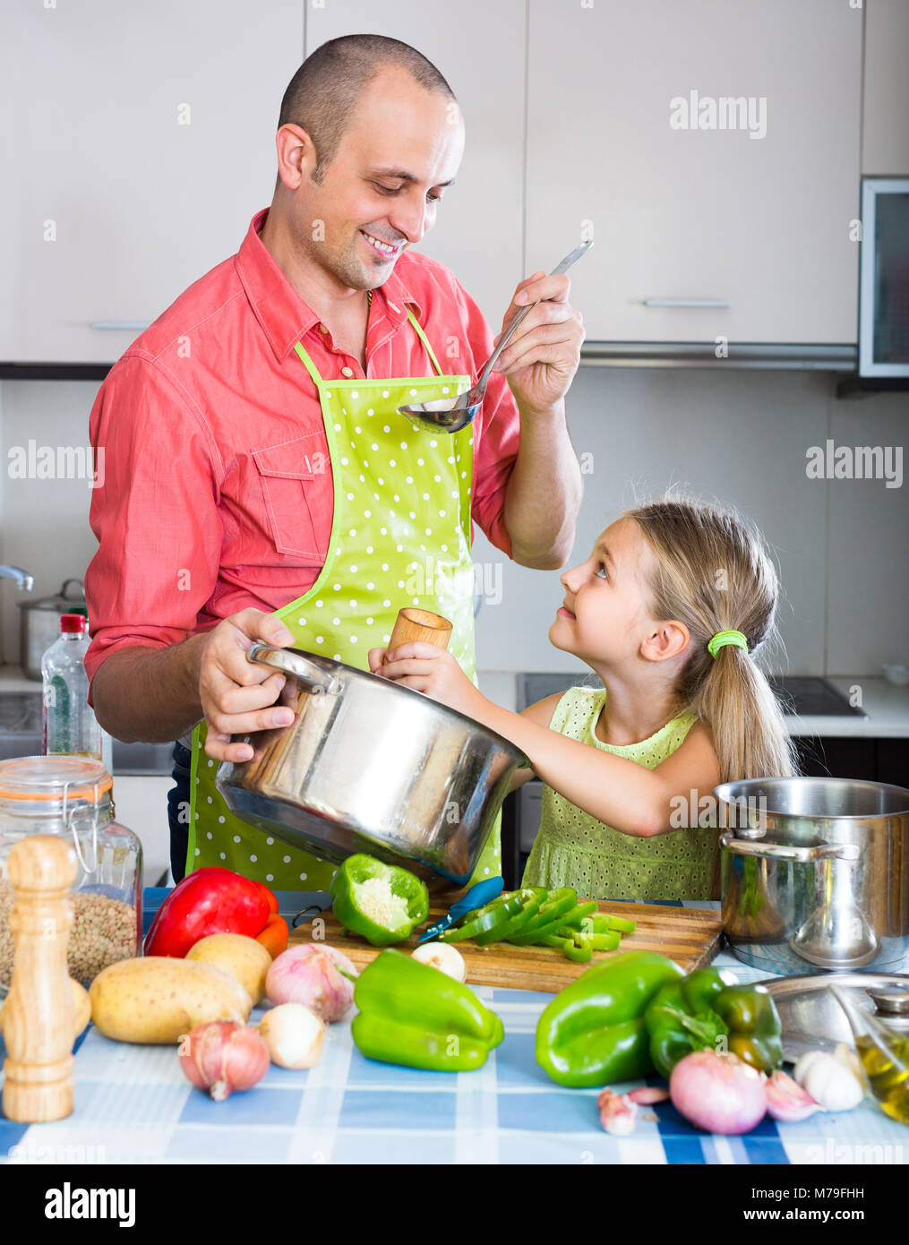 Smiling man and cute little girl cooking vegetables in the kitchen at ...