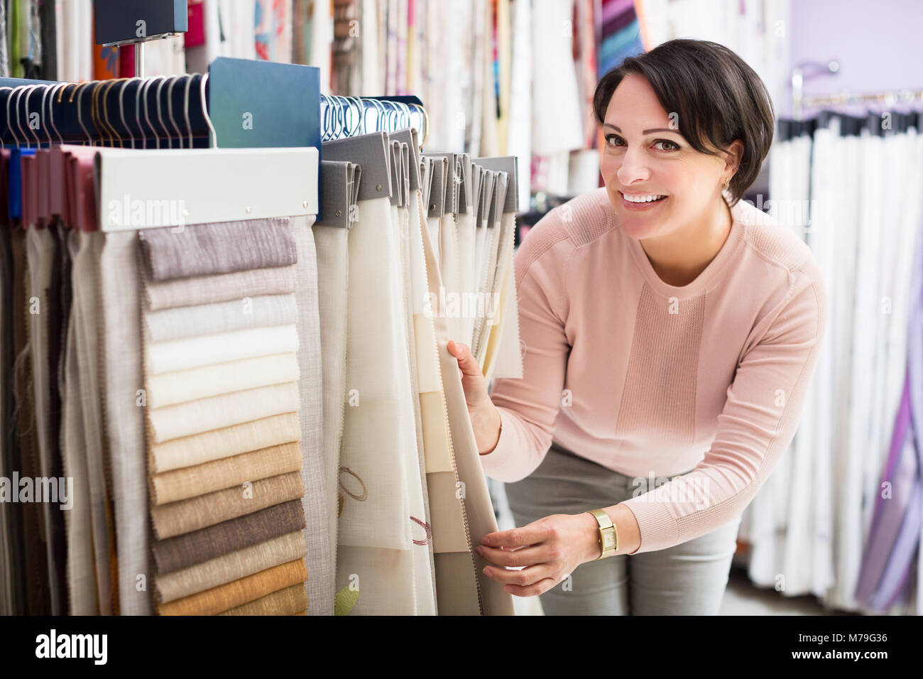 Portrait of positive female customer posing near cloth rolls inside ...