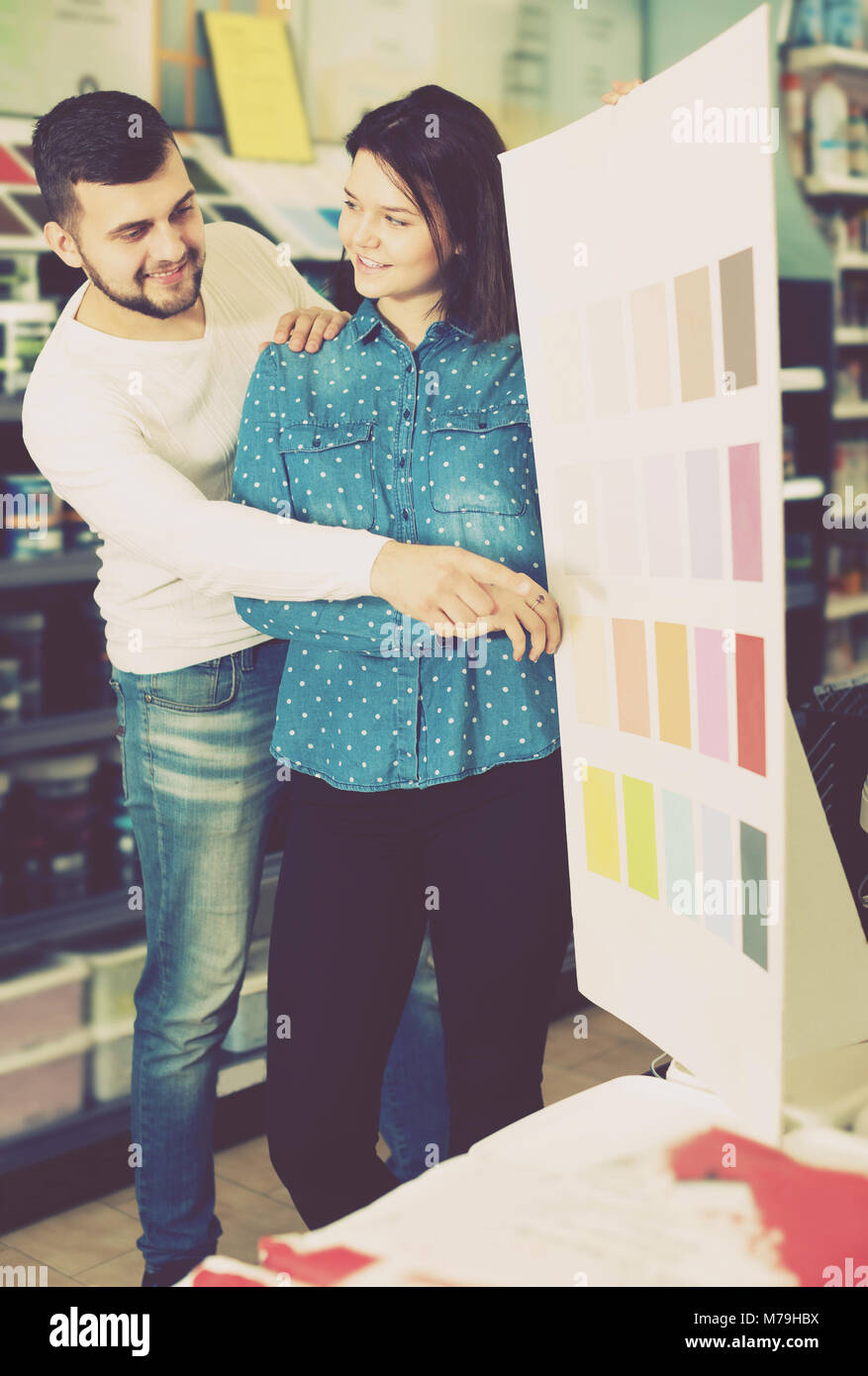 Positive couple examining color scheme variants in paint supplies store ...