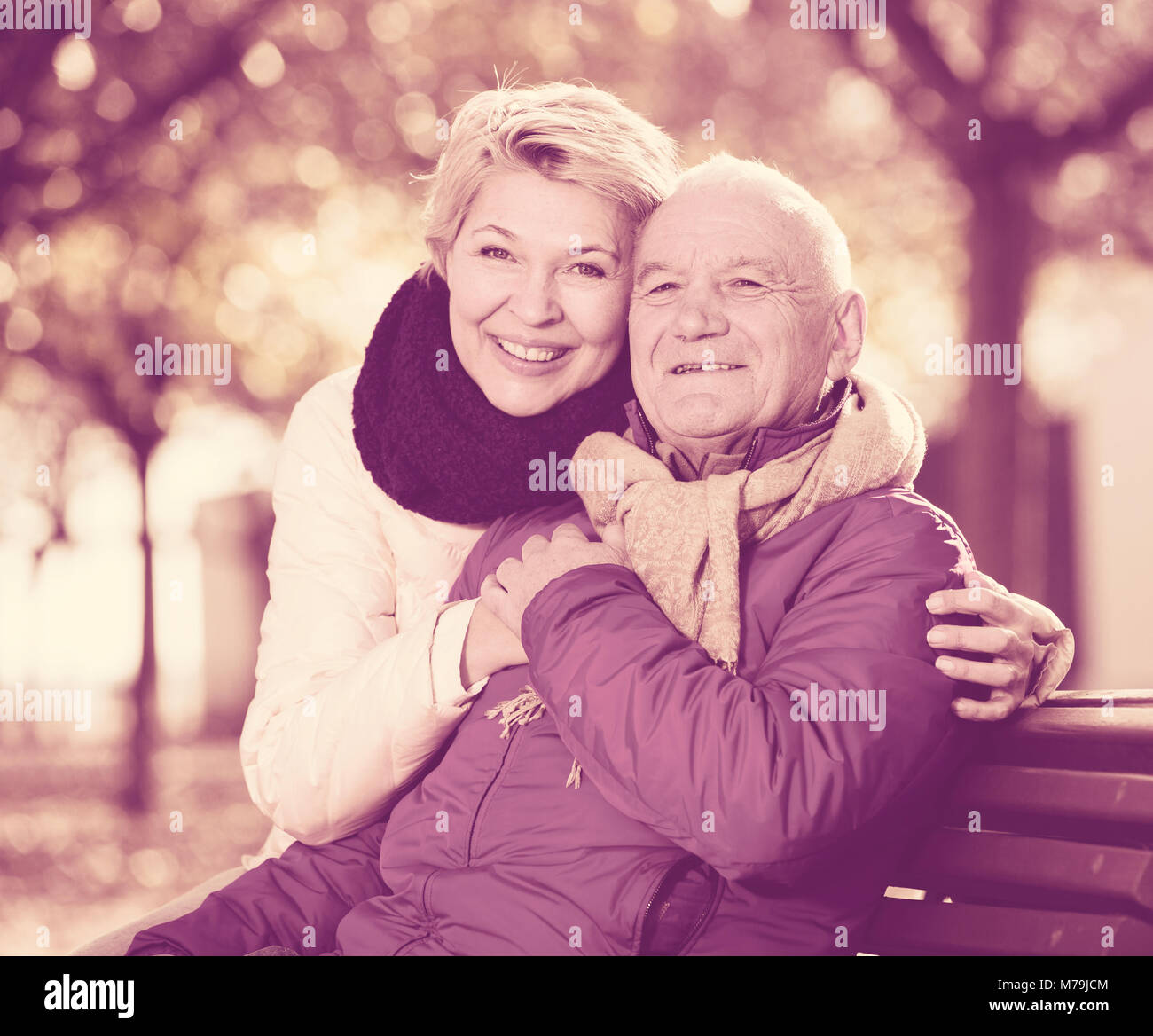 Aged husband and wife sitting together on bench in park on chilly day ...