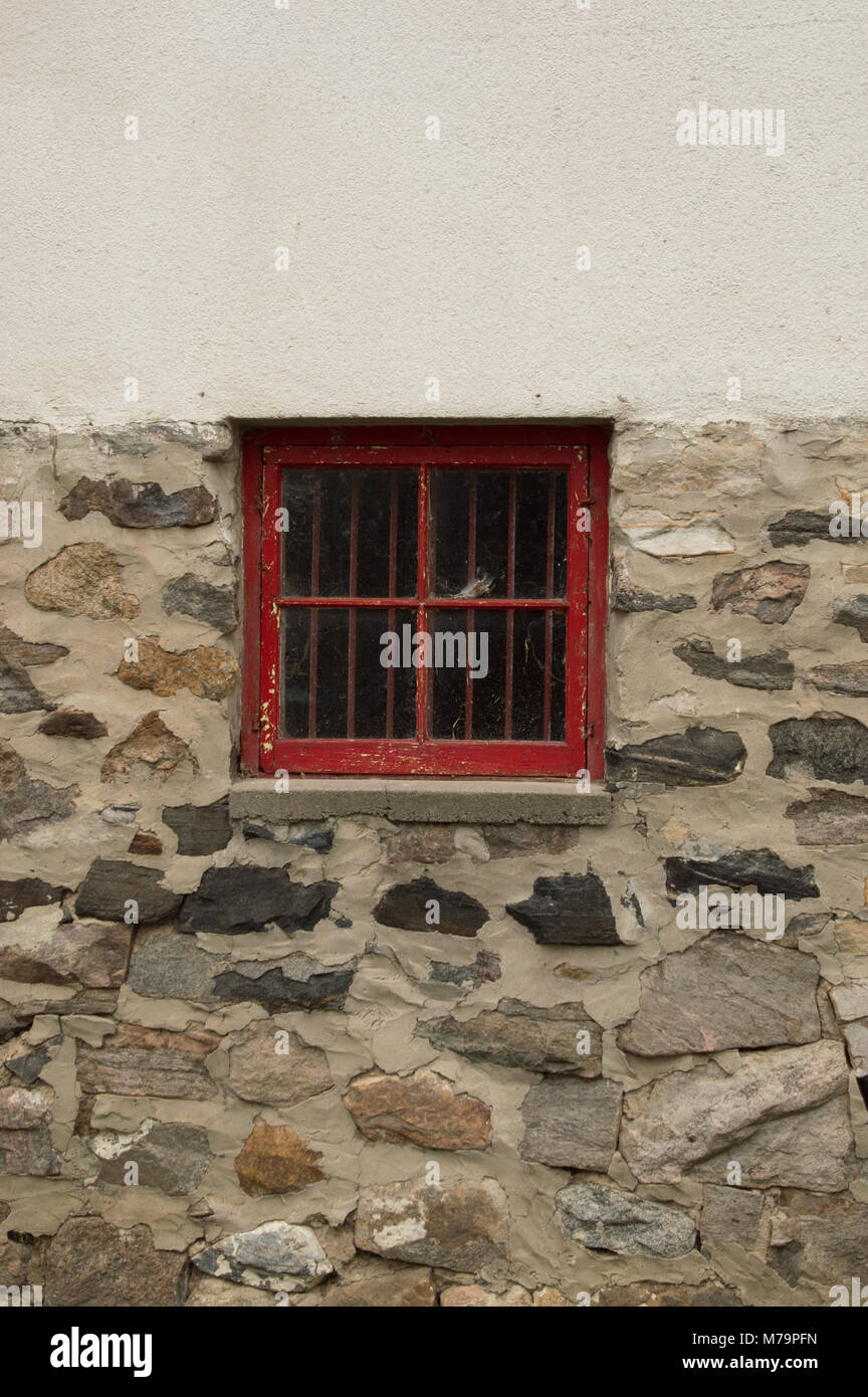 Square red wooden window in a stone and whitewashed wall of an ...