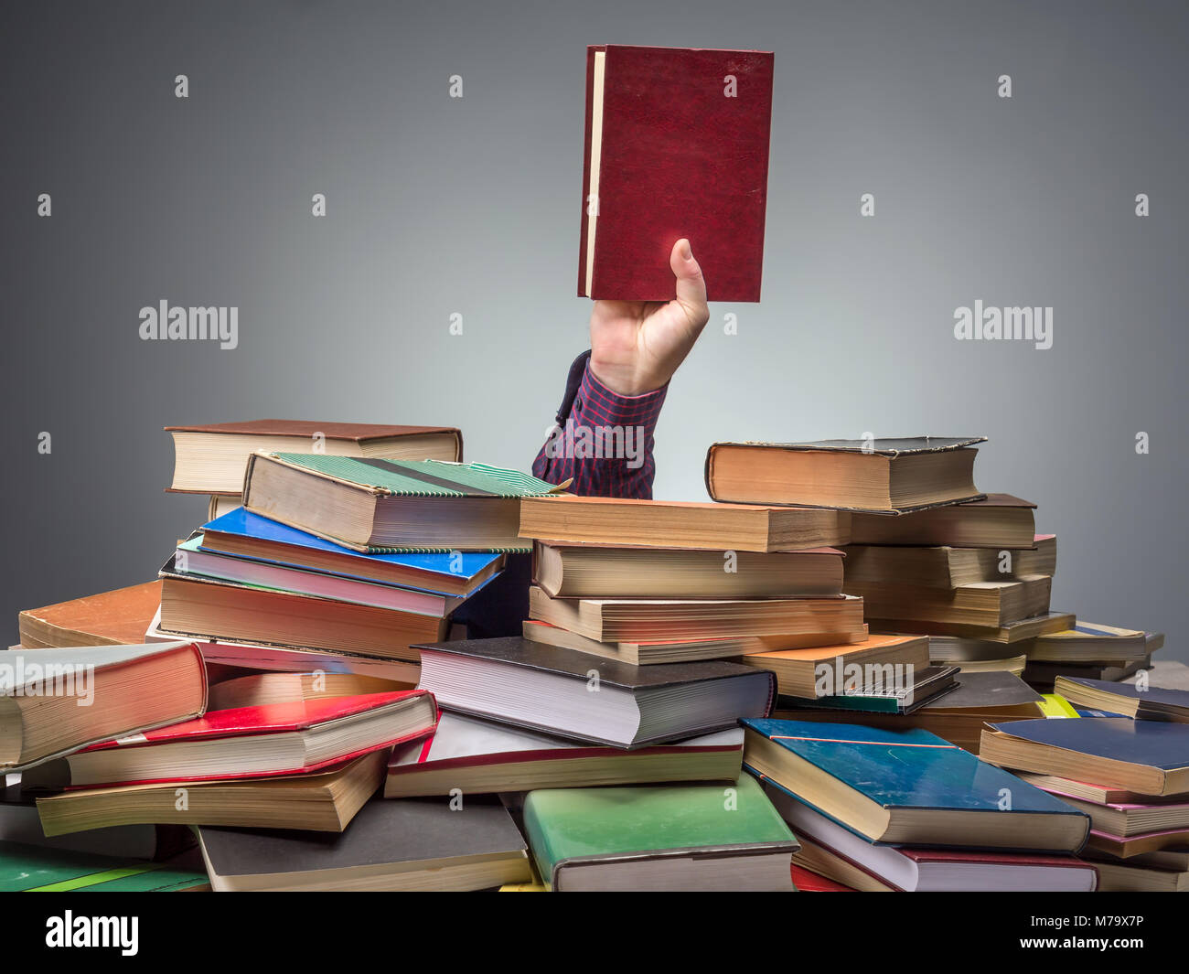 Male hand protruding from pile of books holding the book he was looking ...