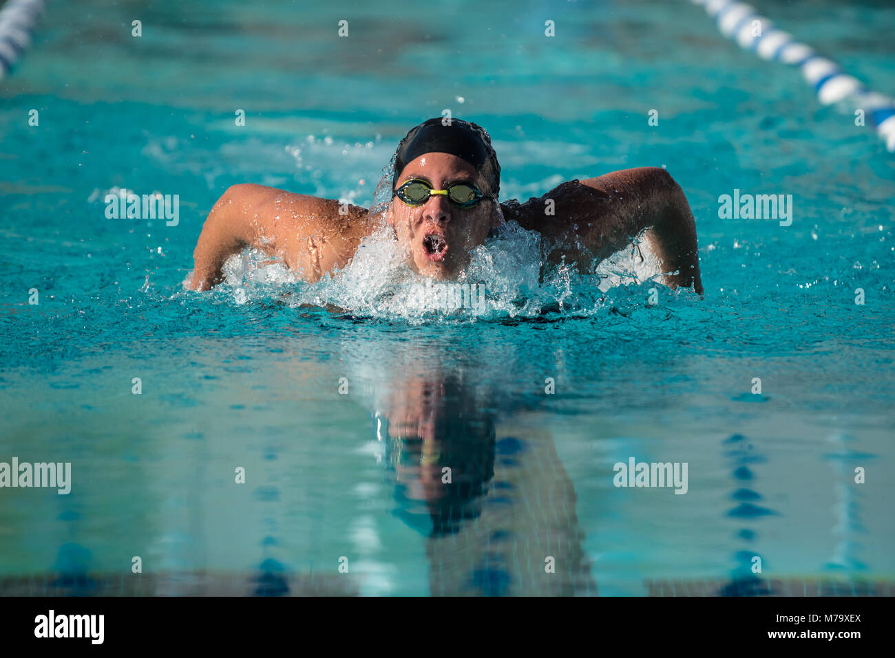 Face and googles of female sprint swimmer reflected in pool water as ...