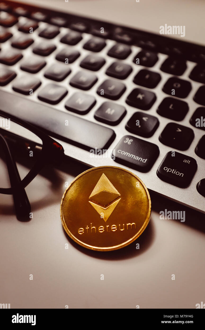 Gold Ethereum coin on computer keyboard backlit with glasses, shallow ...
