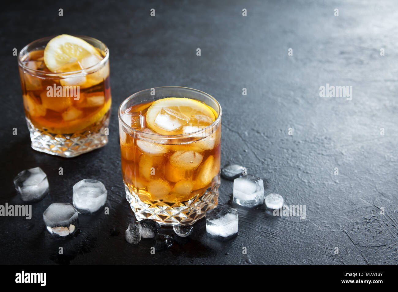 Cold iced tea with lemon and ice cubes over black stone background ...