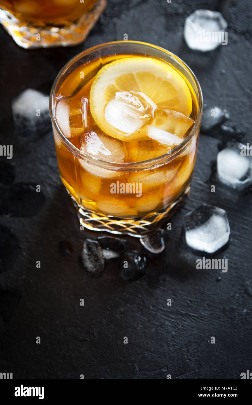 Cold iced tea with lemon and ice cubes over black stone background ...