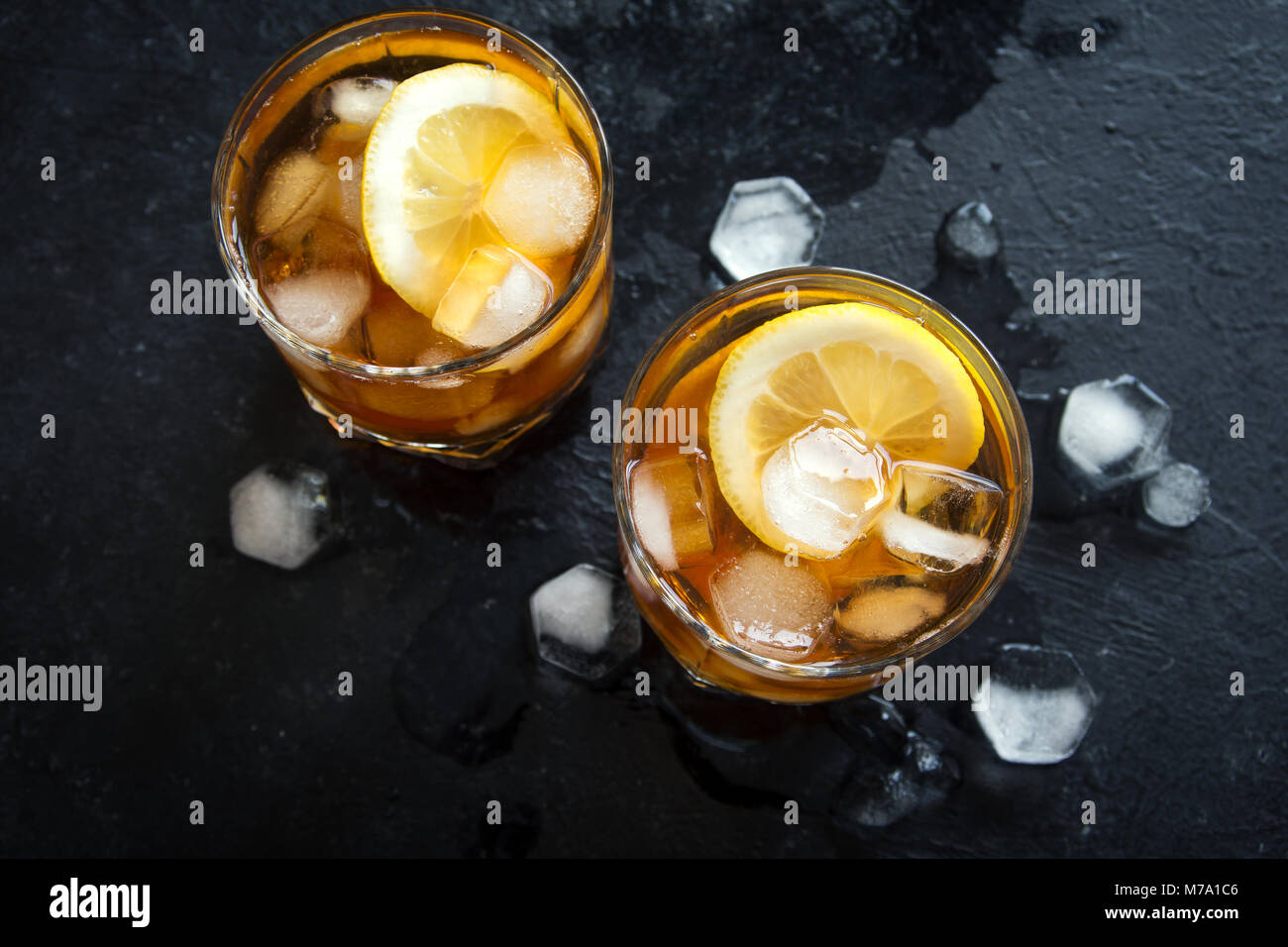 Cold iced tea with lemon and ice cubes over black stone background ...