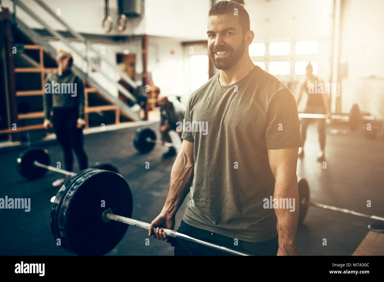 Fit young man in sportswear smiling while lifting heavy weights during ...