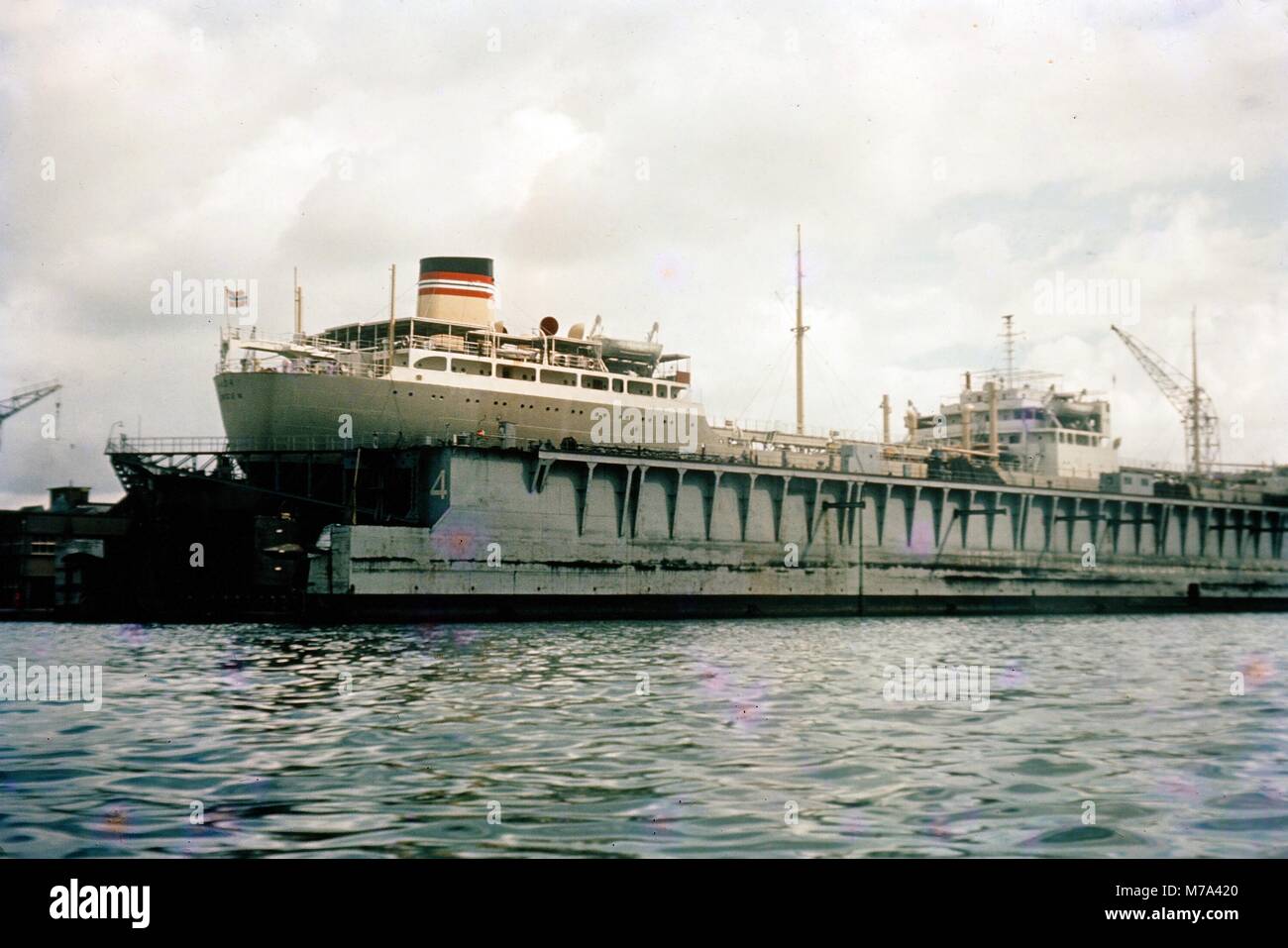 A large ship is held in dry dock in a port, cranes and other equipment ...