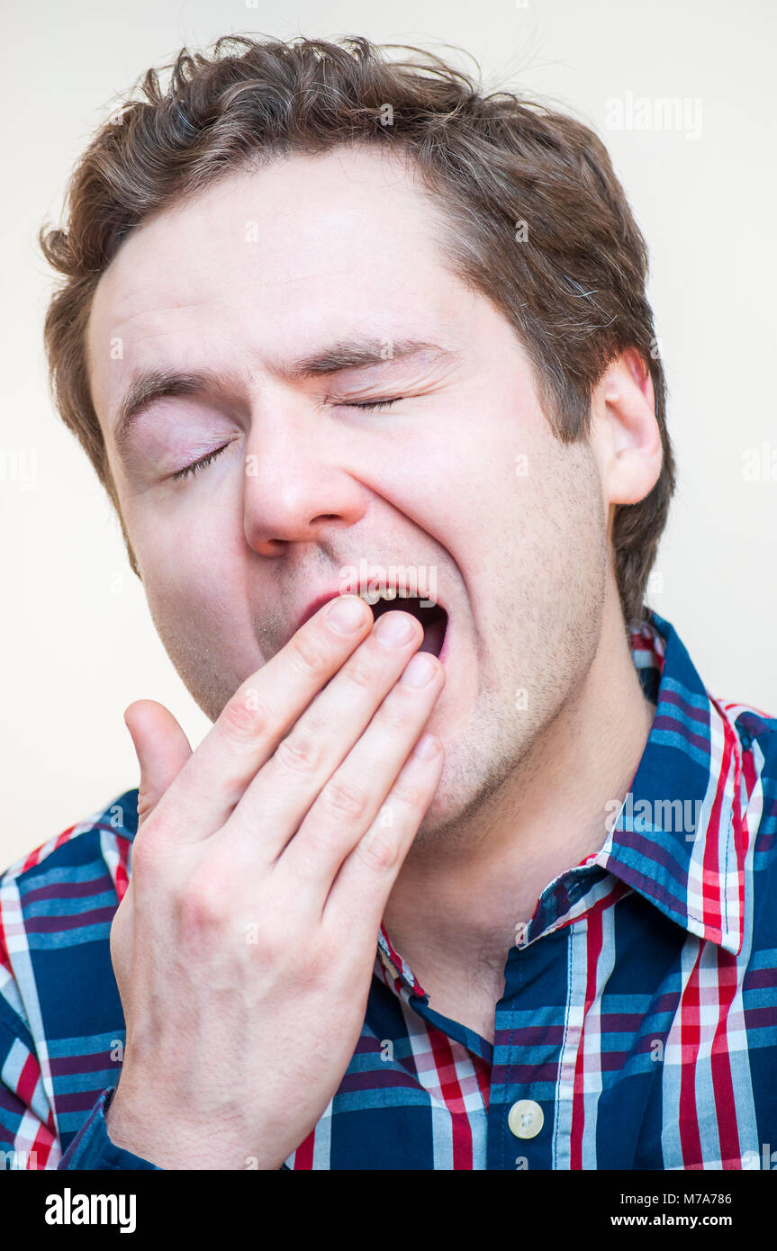 Portrait of young tired yawning curly man covers his open mouth with ...