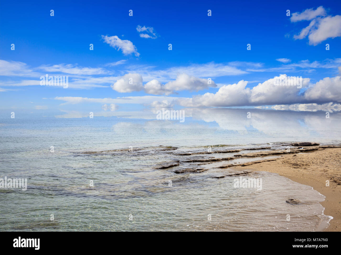 Sandy beach with rocks. Blue sky and calm sea background Stock Photo ...