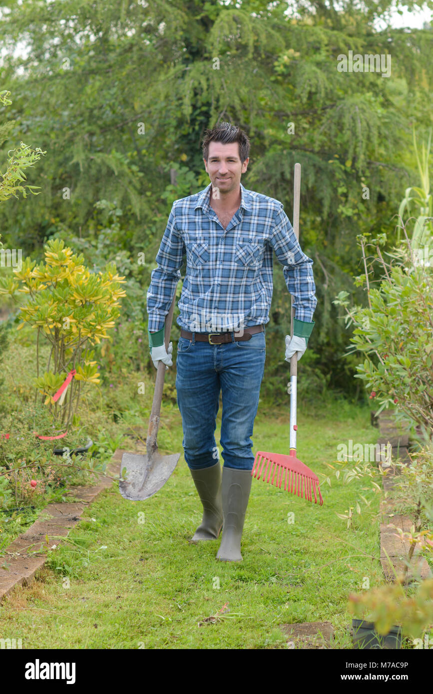 Gardener carrying spade and rake Stock Photo - Alamy