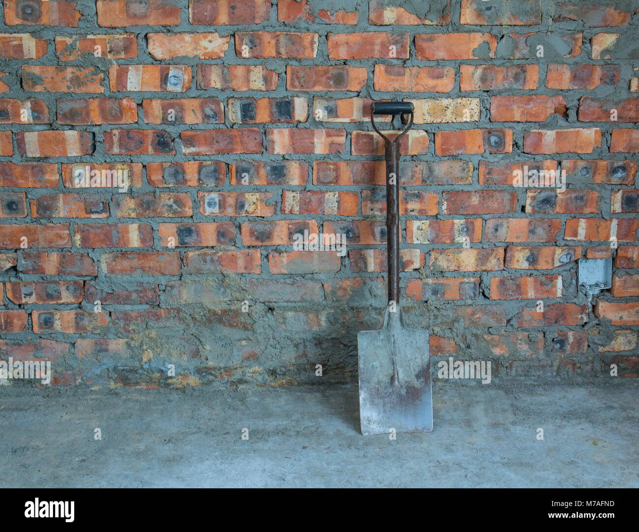 A metal spade rests against a raw brick wall on a building site image ...
