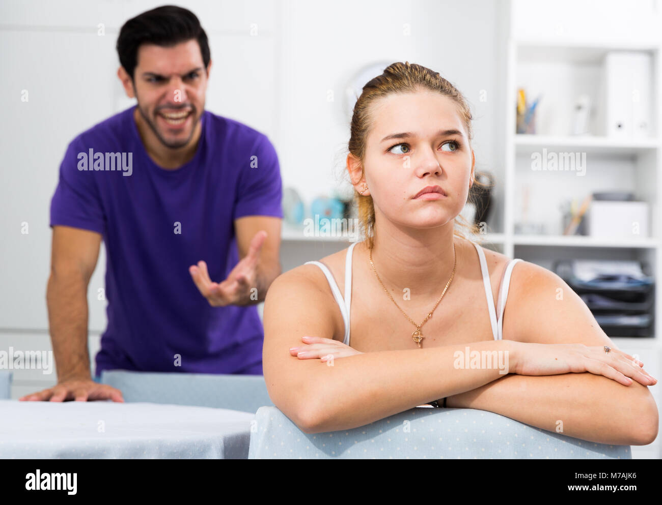 Upset young woman sitting at home table with disgruntled man behind ...