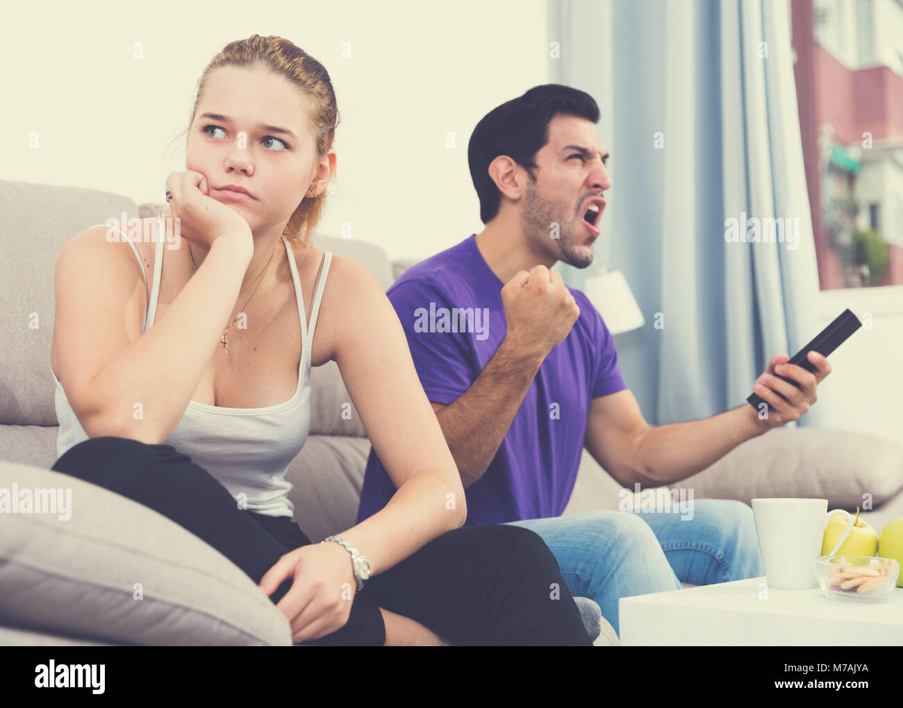 Young man emotionally watching tv and ignoring frustrated girl sitting ...