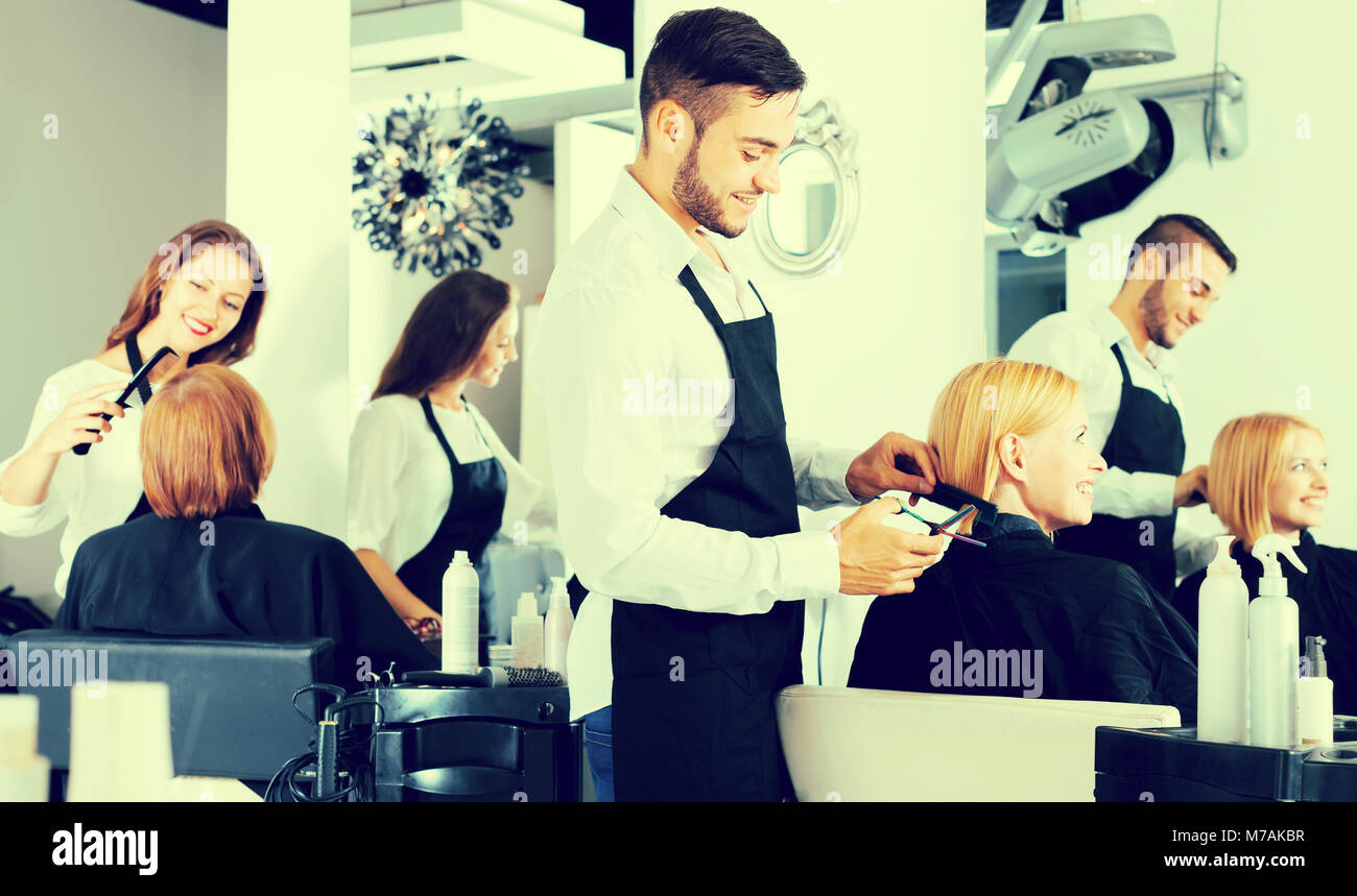 Barber working with hair of young woman in the barbershop Stock Photo ...
