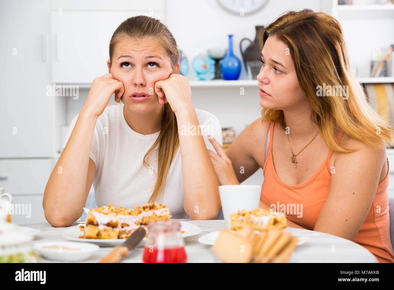 Female talking with young sad friend at the table with cake at home ...