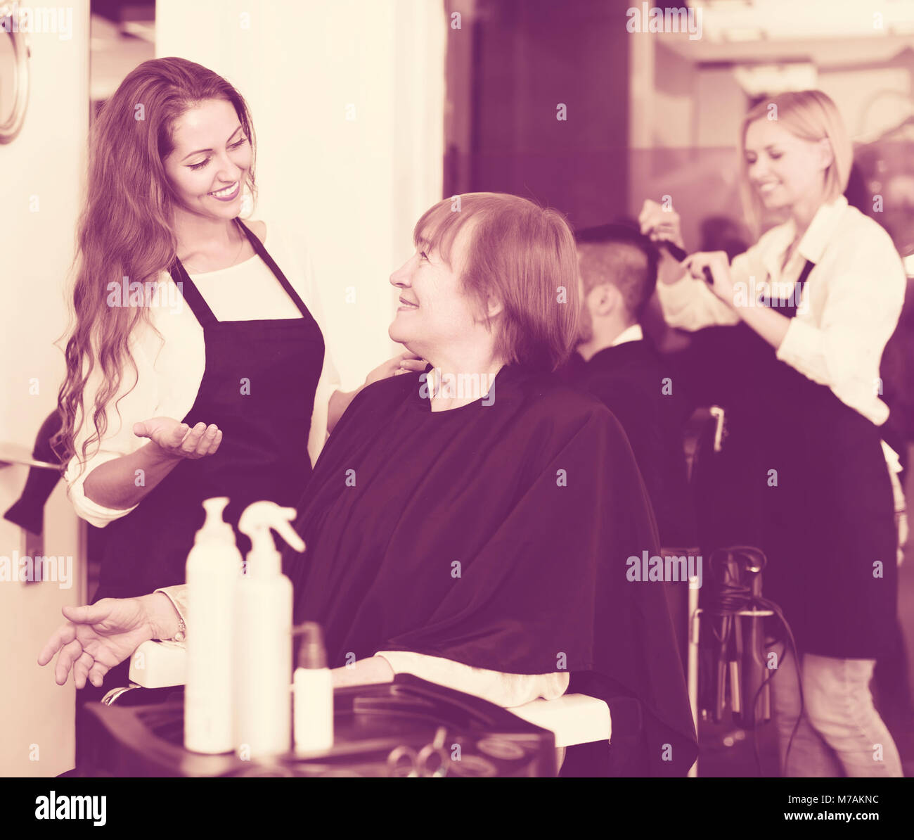 Happy smiling mature woman cutting her hair at the hairdressing salon ...
