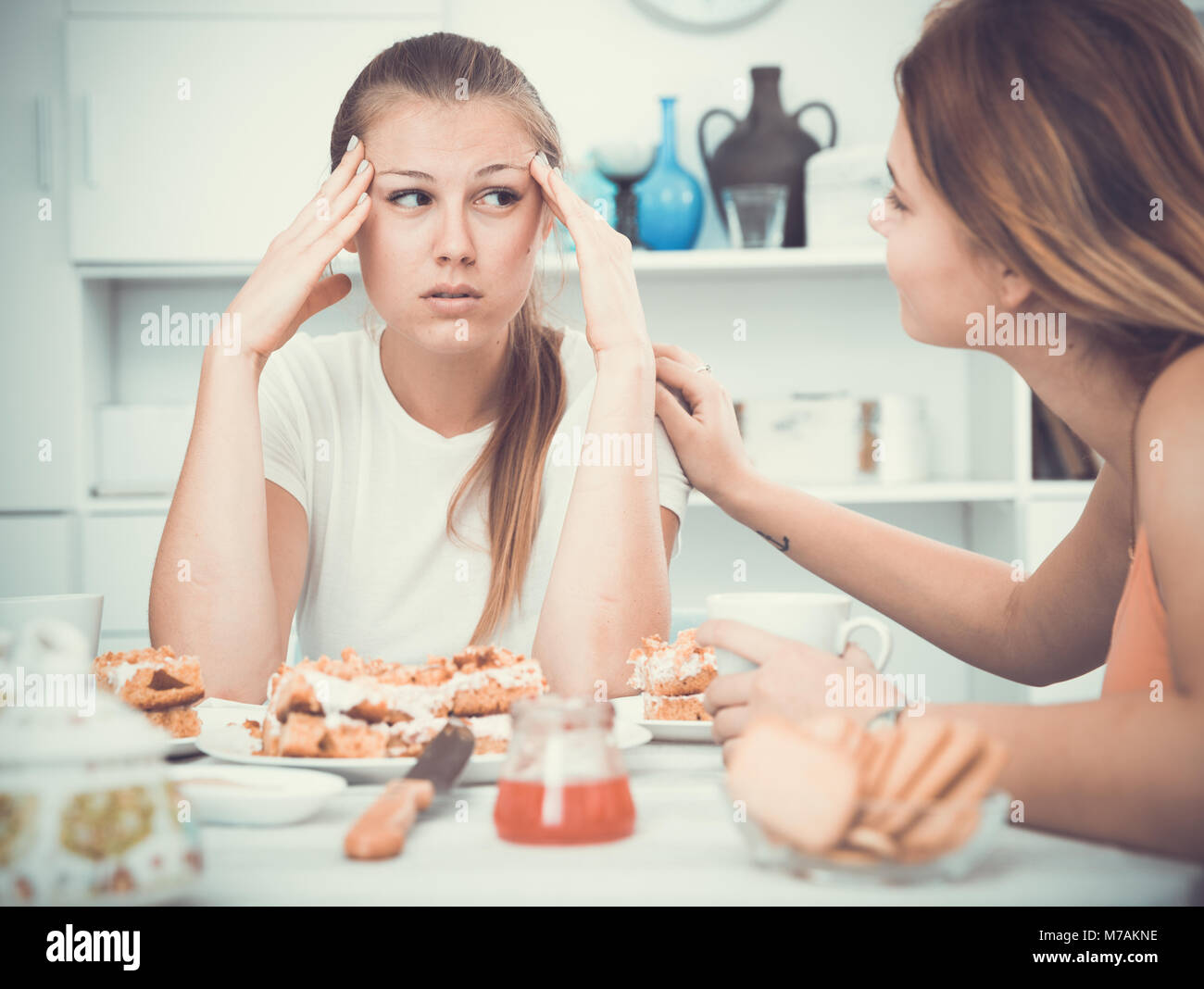 Female talking with young sad friend at the table with cake at home ...