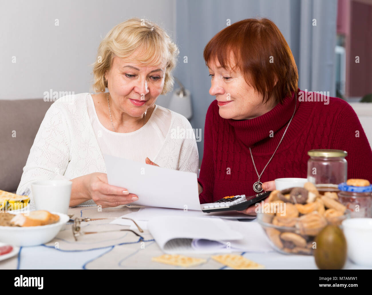 Cheerful elderly women sitting at kitchen table working with documents ...