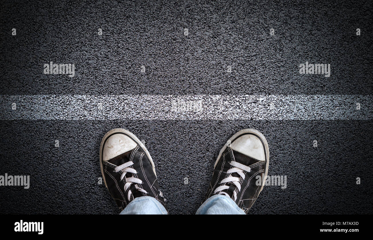 A teenager in jeans and canvas shoes standing on asphalt road behind a ...