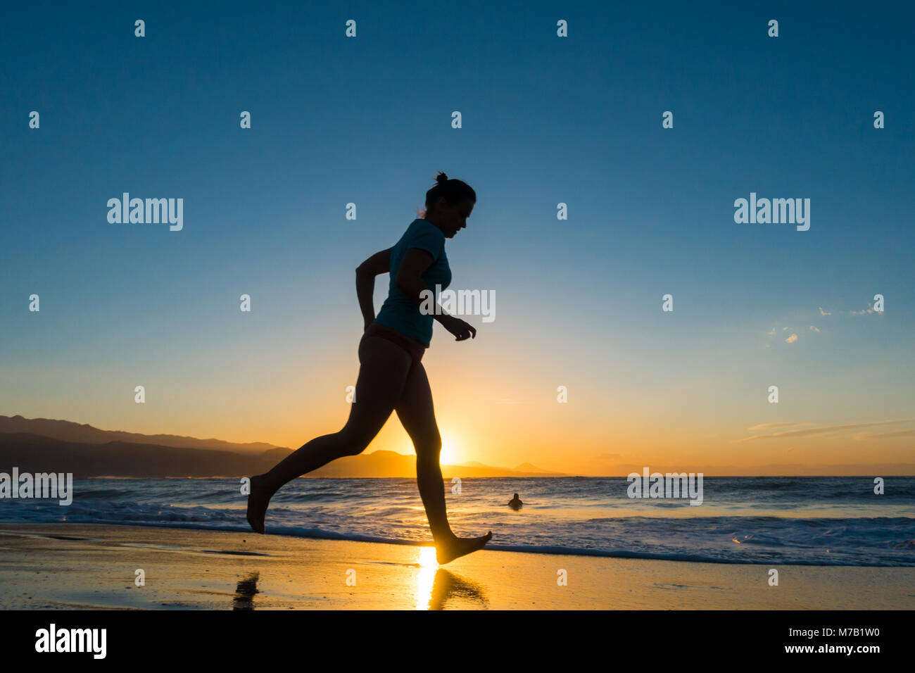 Woman jogging on beach at sunset Stock Photo - Alamy