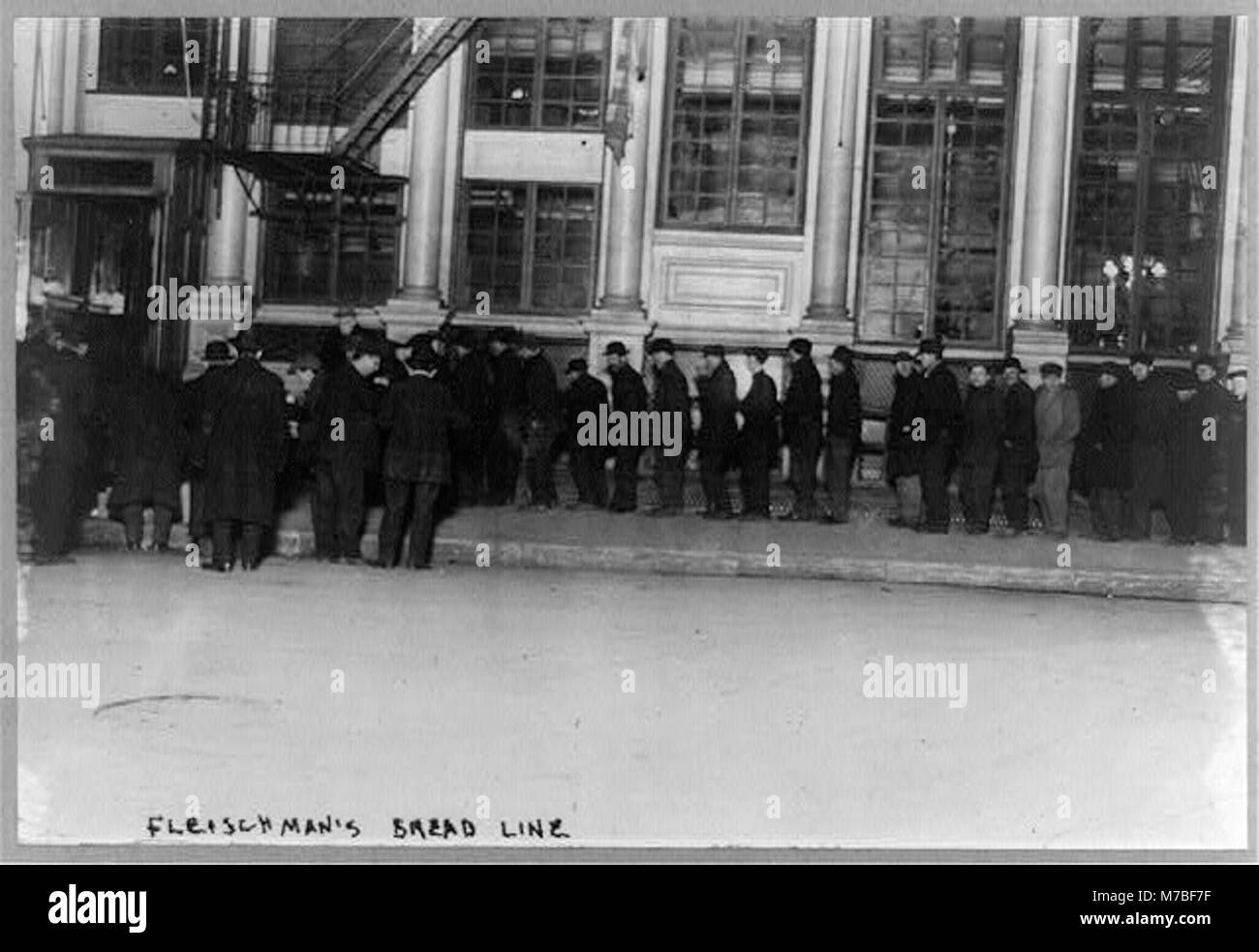 A historical photograph of Bowery men waiting in line for bread at ...