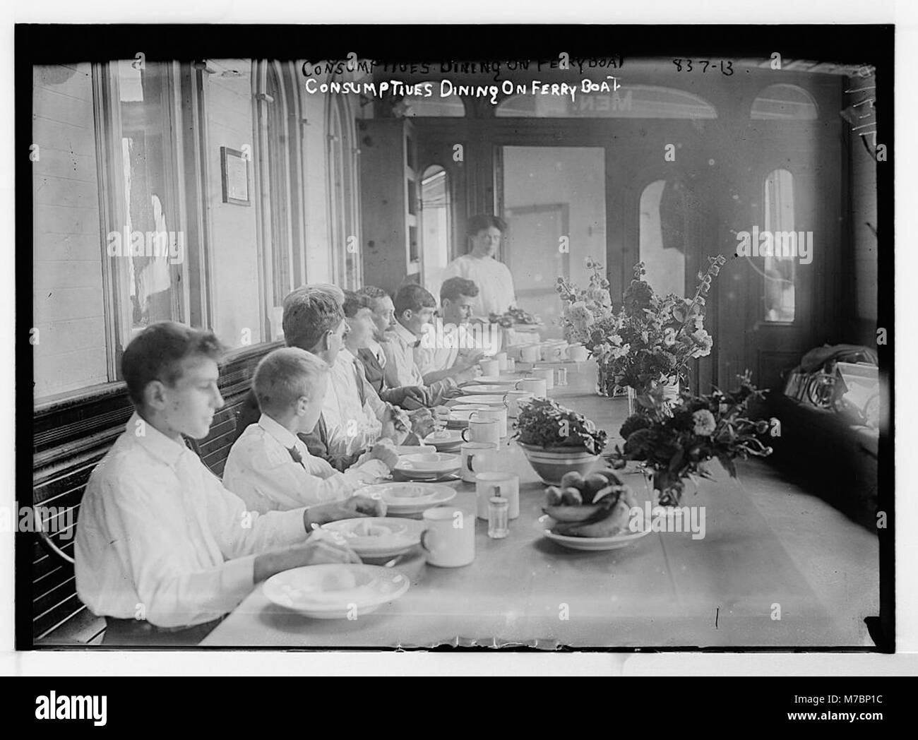 The photograph depicts consumptives (tuberculosis patients) dining on a ...