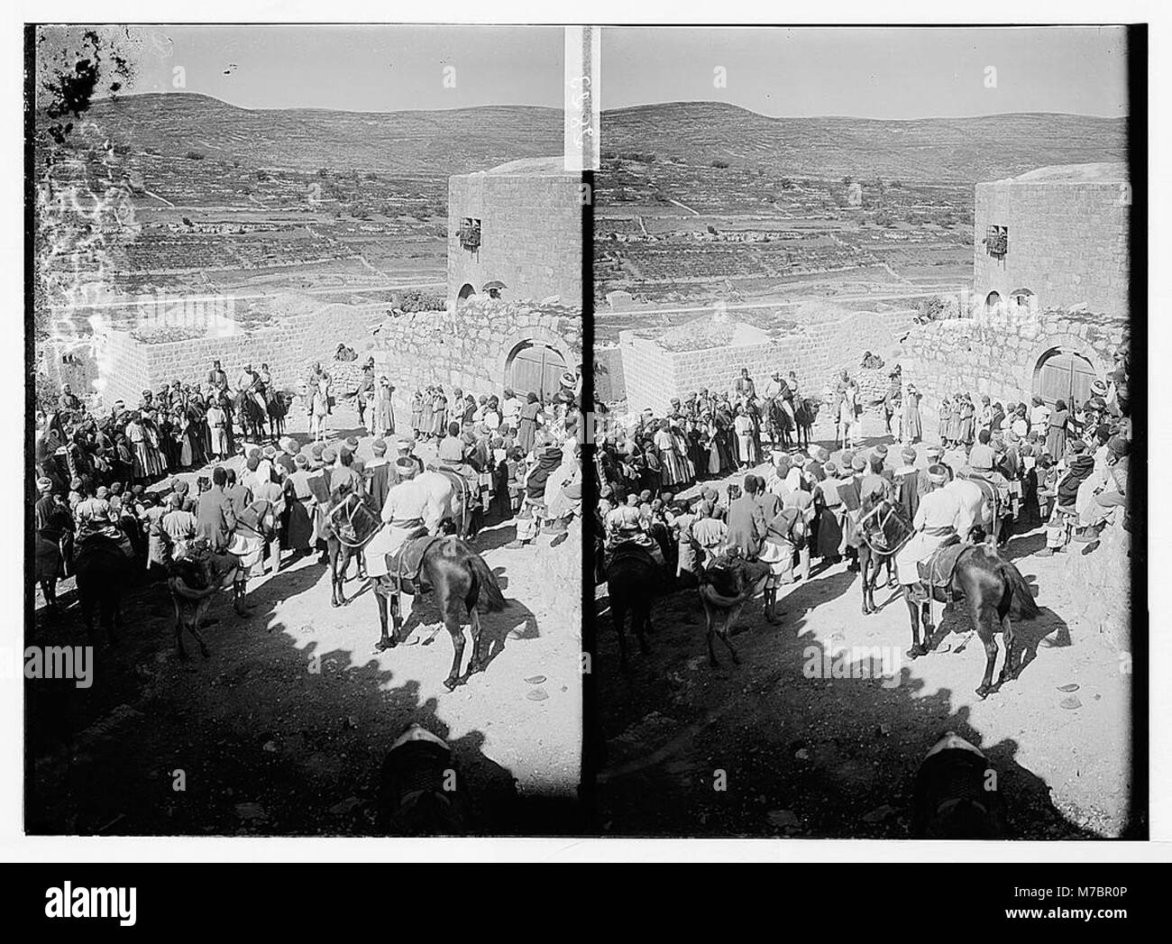 A crowd gathered on a village hill, observing a man on a house with a ...