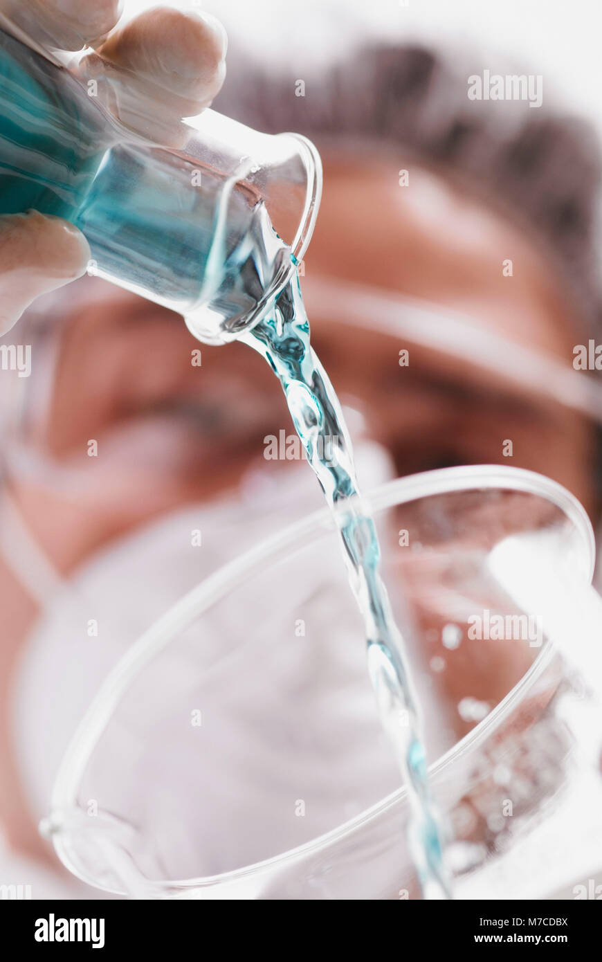 Close-up of a person pouring liquid from a conical flask into a beaker ...