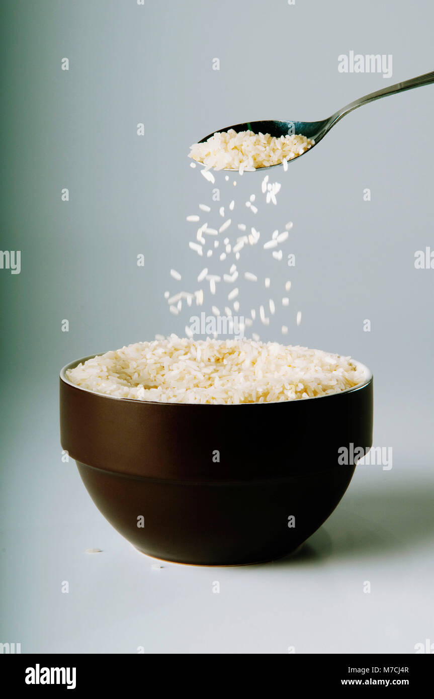 Uncooked rice being poured into a bowl from a spoon Stock Photo - Alamy