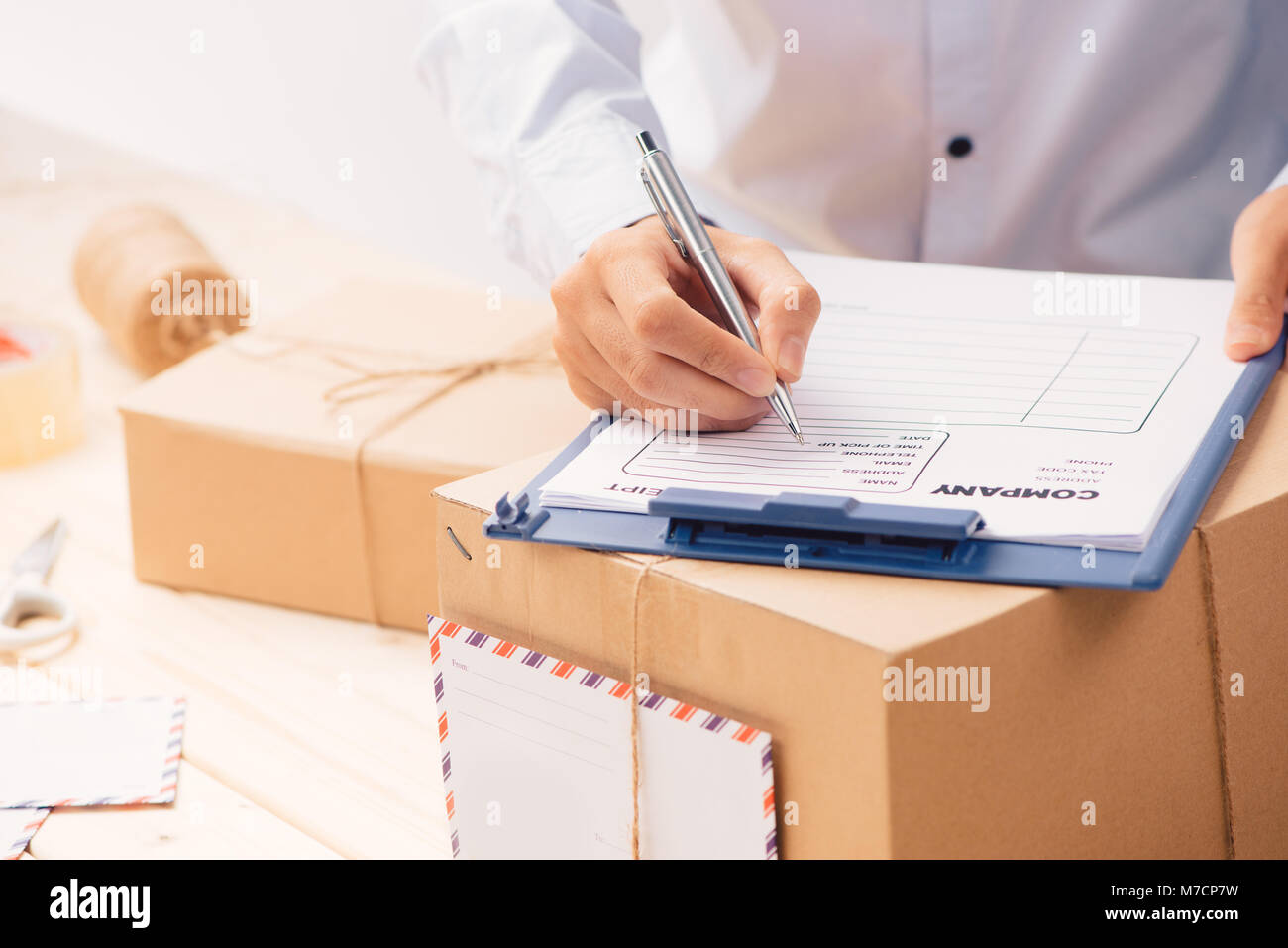 Courier making notes in delivery receipt among parcels at table Stock ...