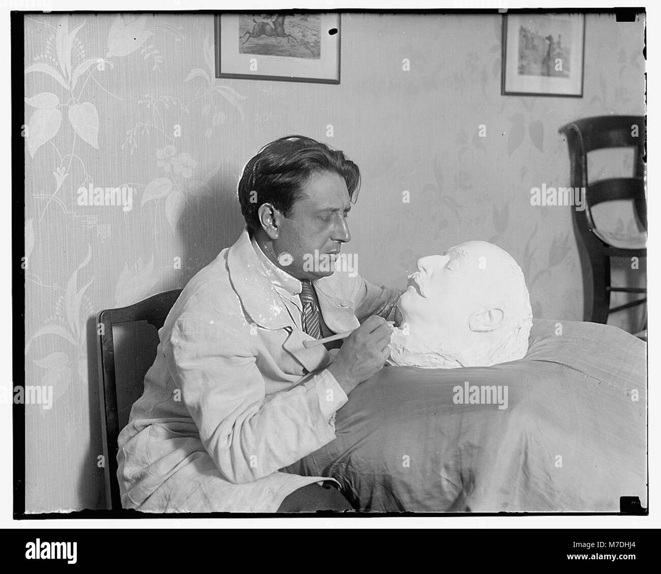 The image shows a man sculpting a plaster head, a process that ...