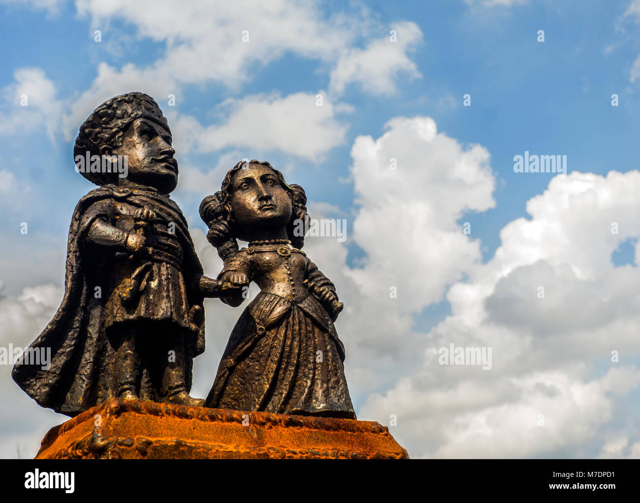 Copper sculpture of the medieval couple against a blue sky with clouds ...