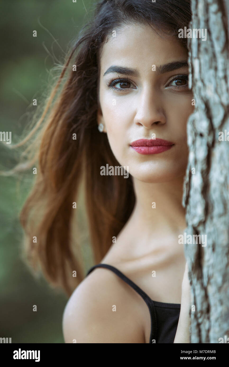 Beautiful young woman hiding behind a tree Stock Photo - Alamy