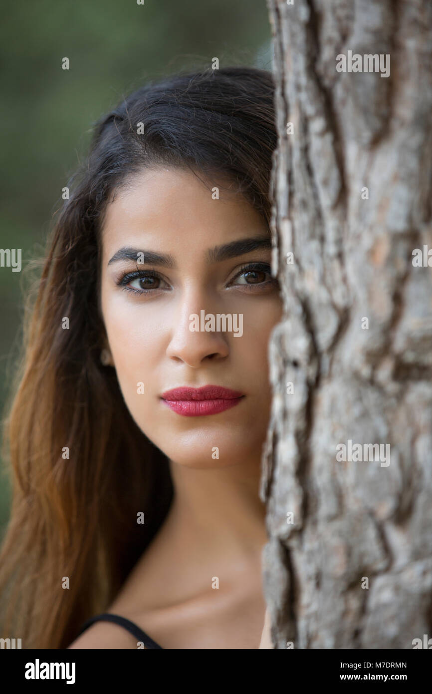 Serious young woman hiding behind a tree Stock Photo - Alamy